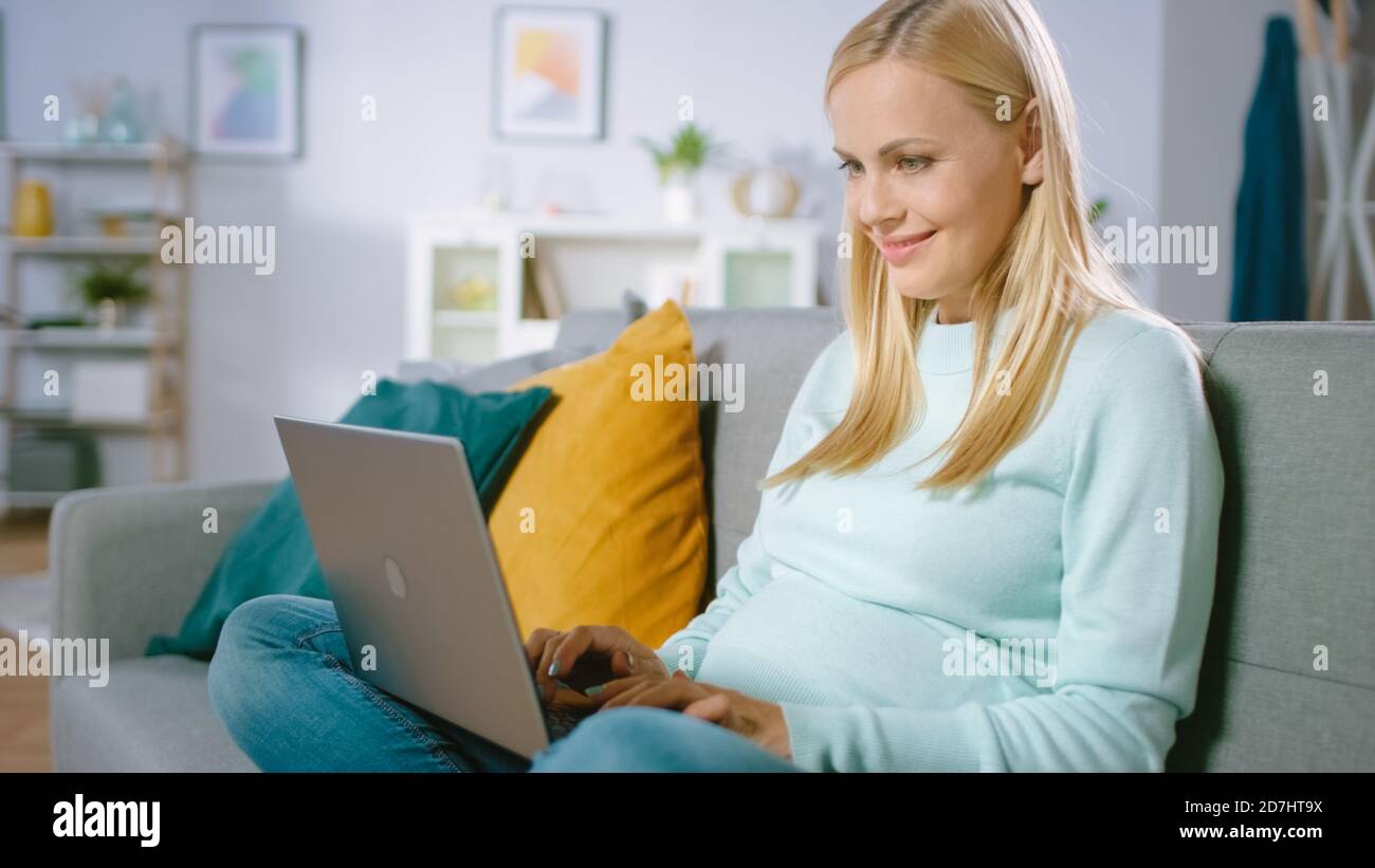 Happy Pregnant Woman Resting on a Sofa Uses Laptop Computer. Smiling ...