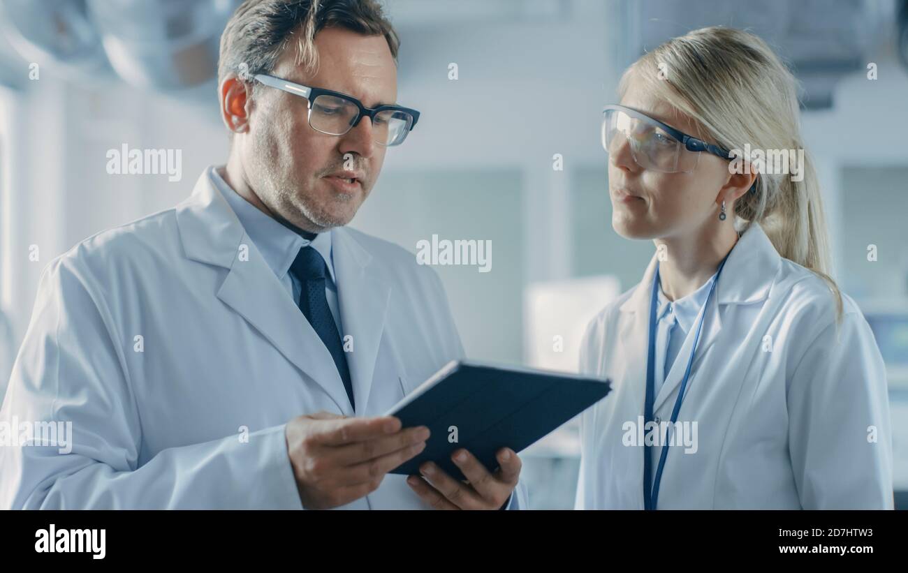 Male and Female Research Scientists Talking, Using Digital Tablet ...