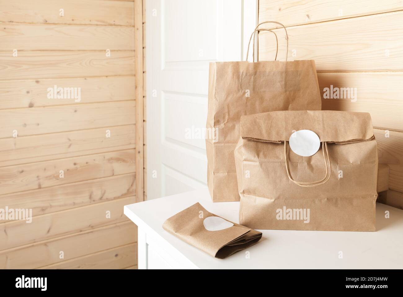 Paper bags with blank white stickers stand on a table in wooden room ...