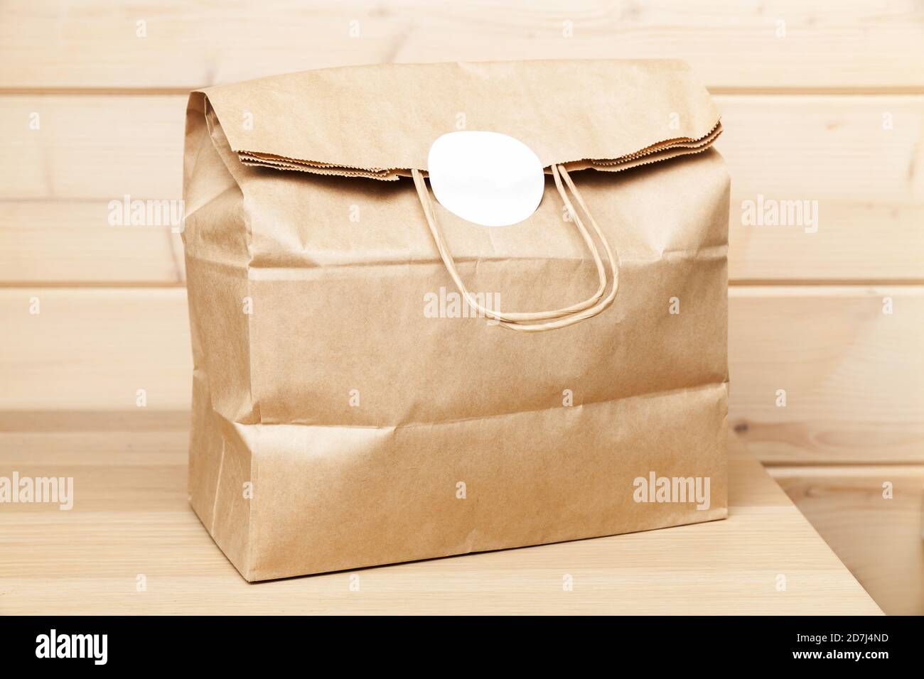 Full paper bag with white sticker stands on a table in wooden room ...
