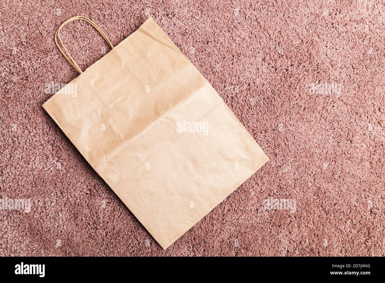 An empty flat paper bag lays on pink carpet, top view photo background ...