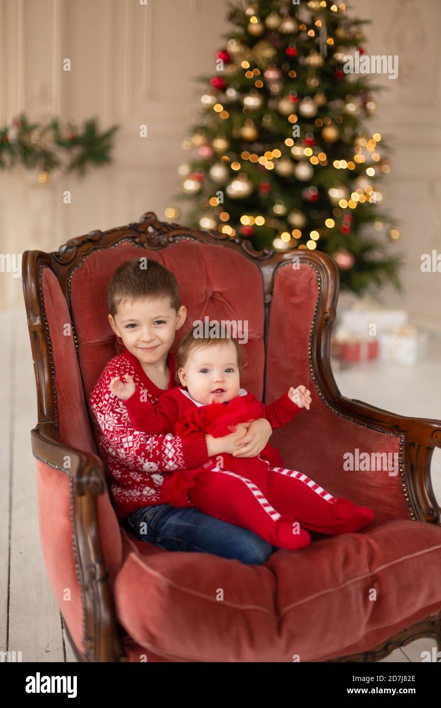 Litttle brother hugs his little sister in red retro chair near ...