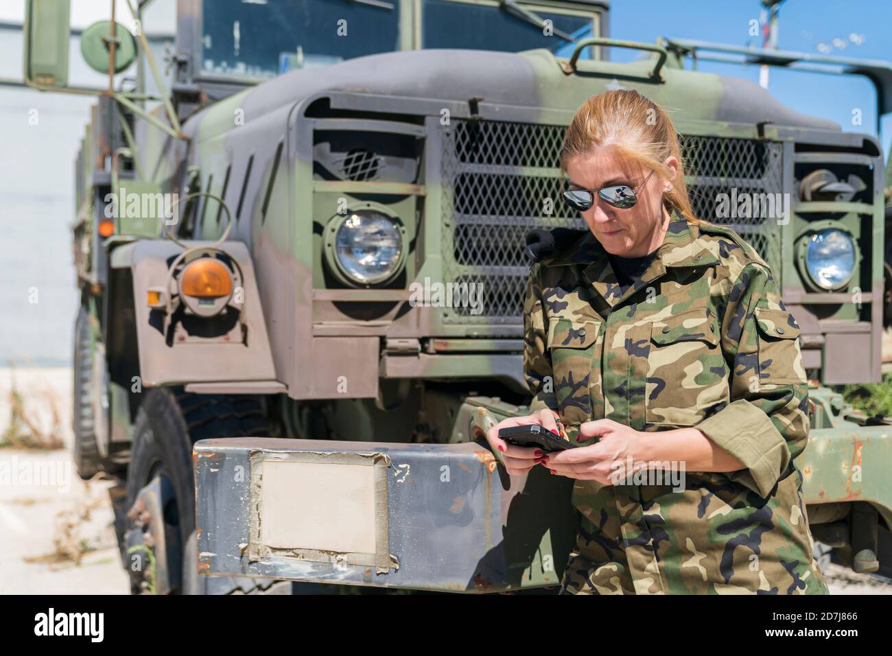 Mature blond female army soldier text messaging through smart phone ...