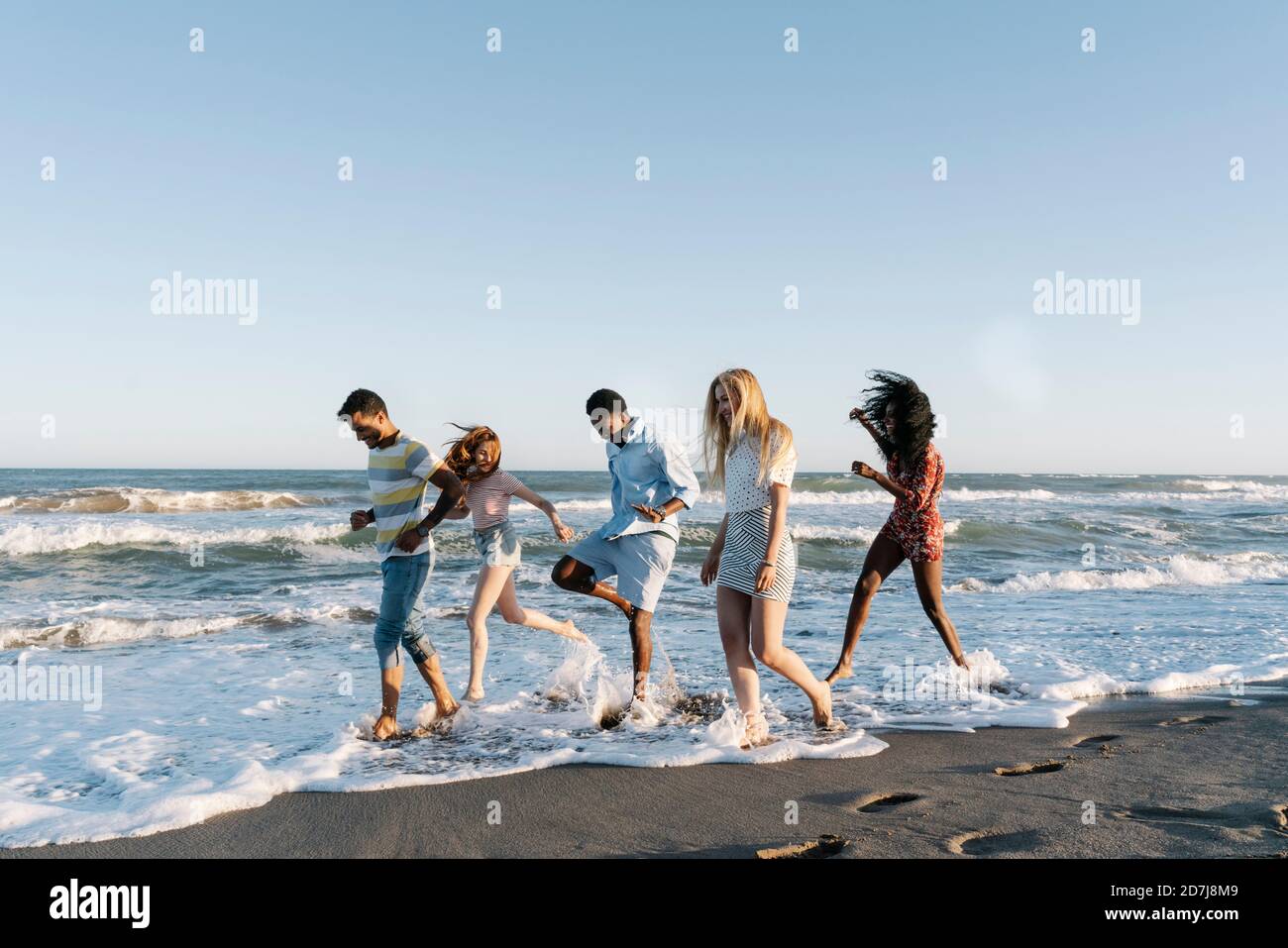 Young friends playing in water on beach during sunny day Stock Photo ...