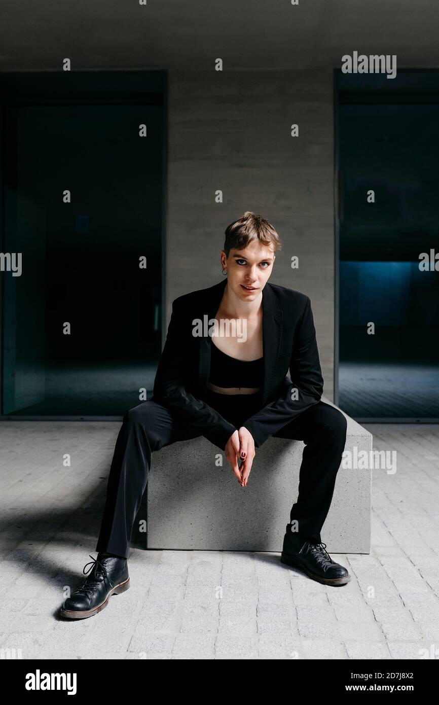 Confident trans young man wearing black suit sitting on seat in ...