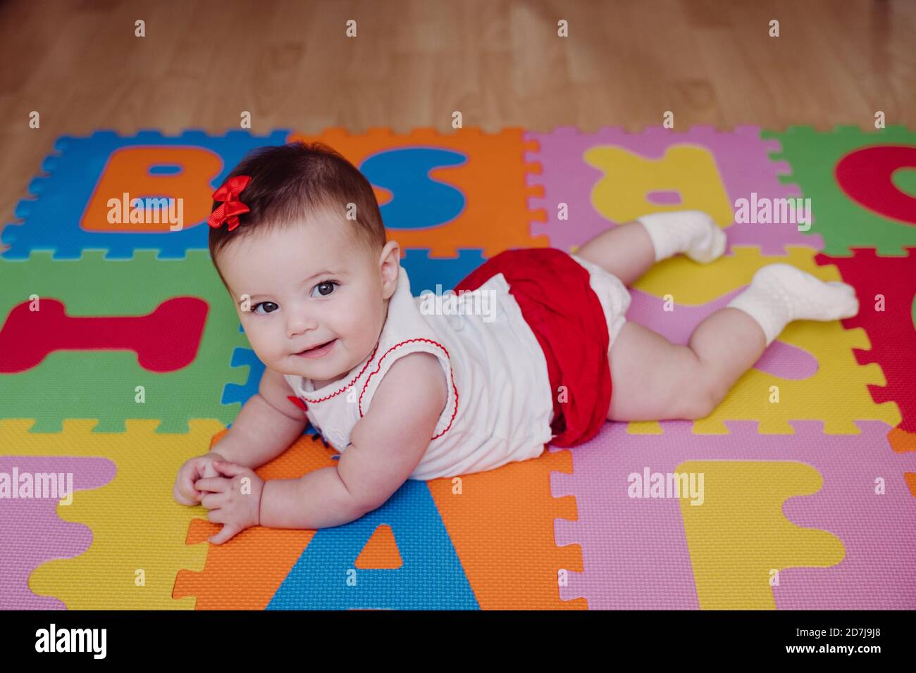 Cute smiling baby girl lying on colorful puzzle playmat at home Stock ...
