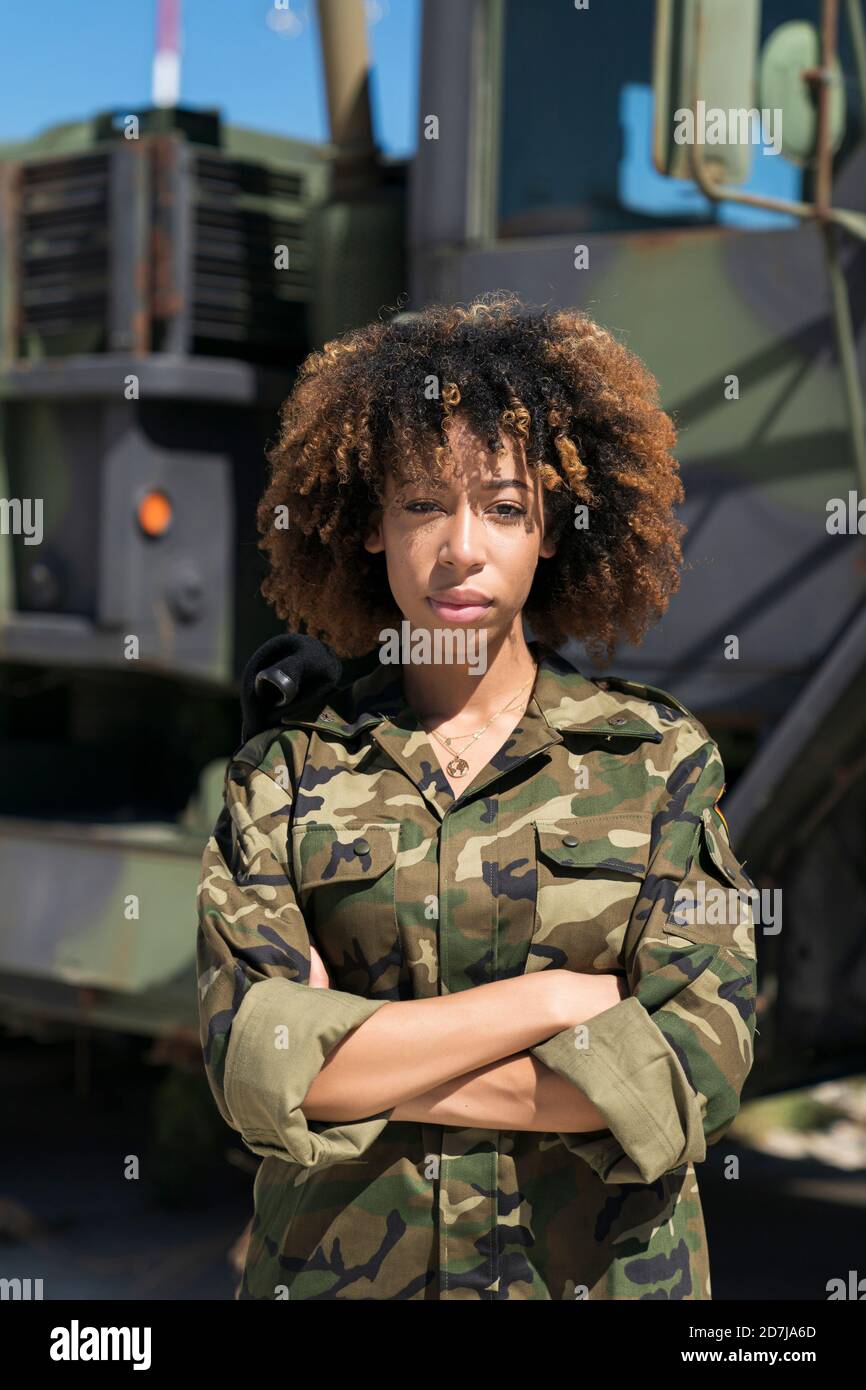 Confident young female army soldier with arms crossed standing against ...