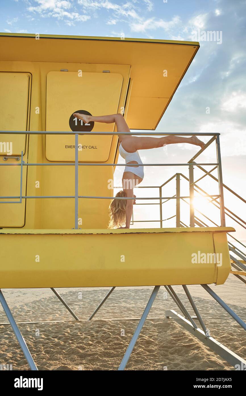 Woman stretching her legs while practicing handstand at lifeguard hut ...