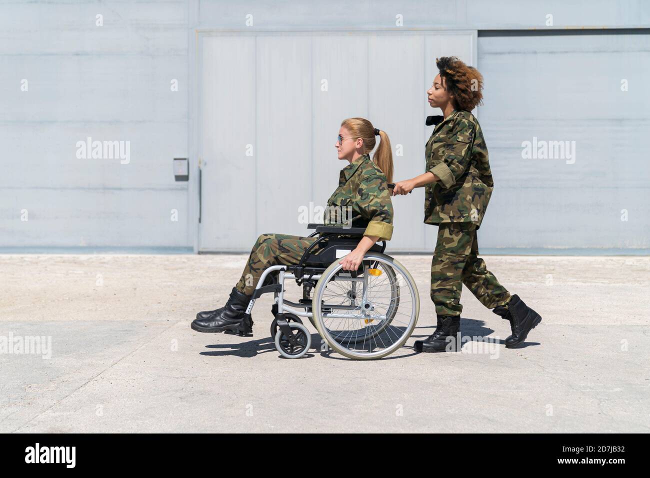 Young female military soldier pushing mature colleague on wheelchair at ...