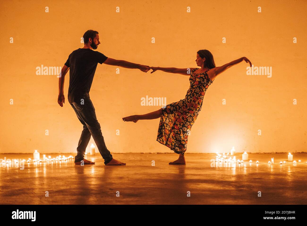 Couple holding hands while dancing by lit candles against wall in ...