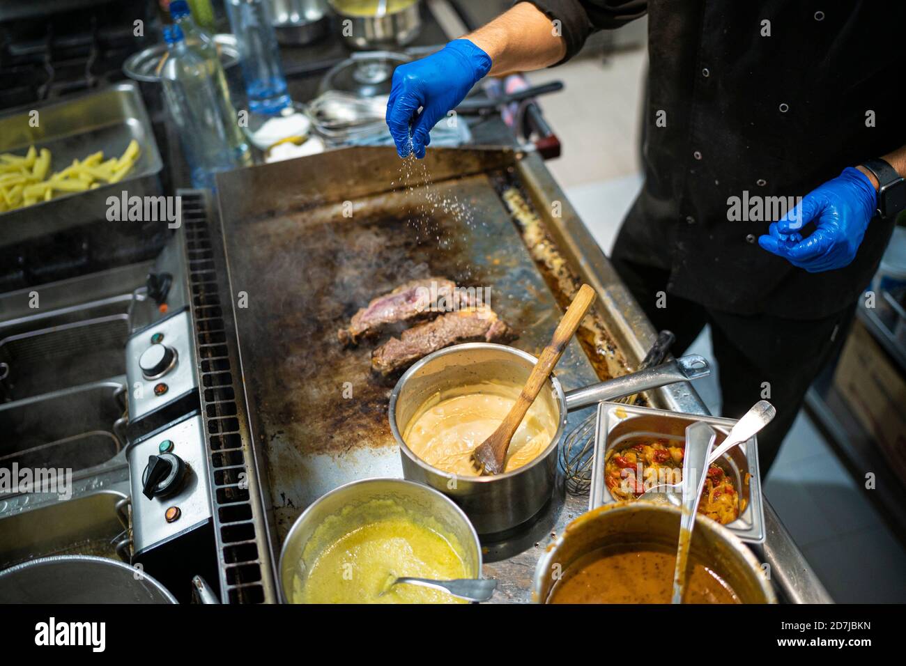 Man sprinkling salt on meat while standing by gas stove at commercial ...