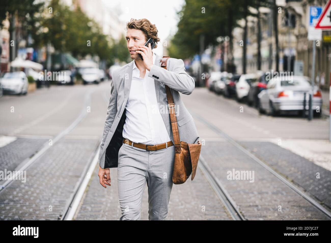 Man with bag talking on mobile phone while walking at tramway in city ...