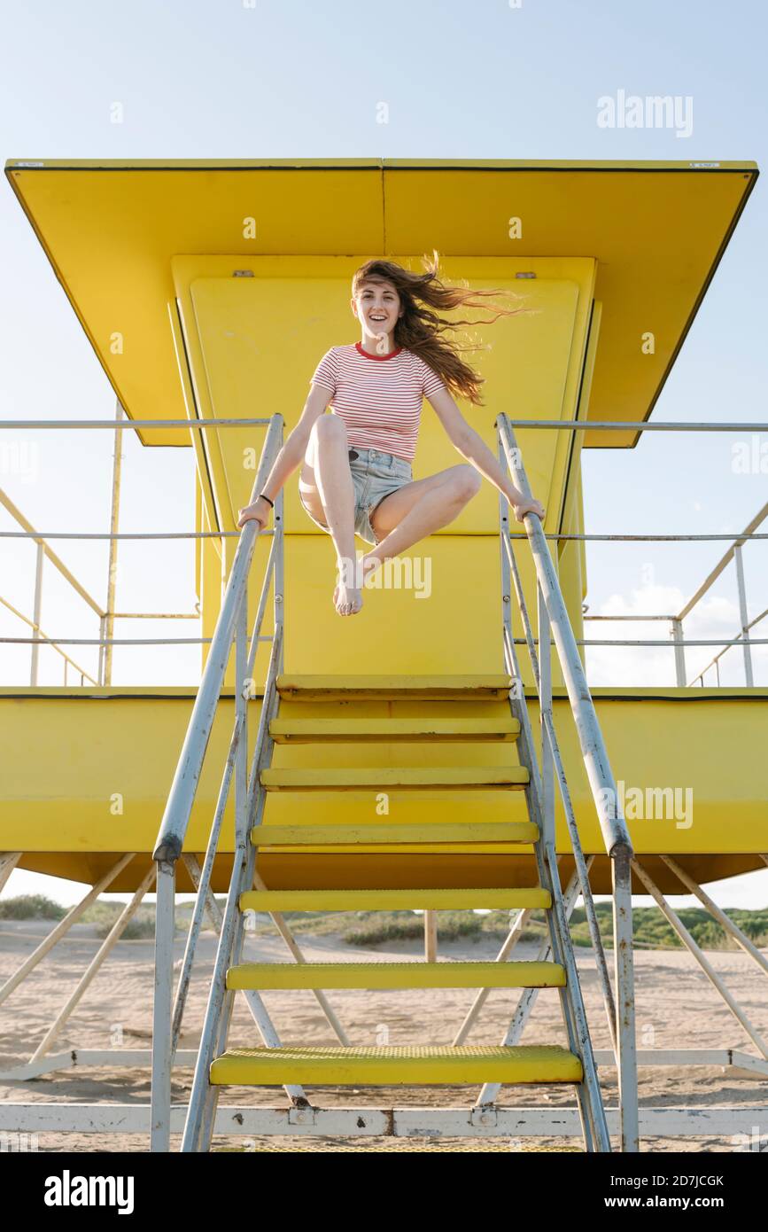 Cheerful young woman jumping on steps of lifeguard hut at beach Stock ...