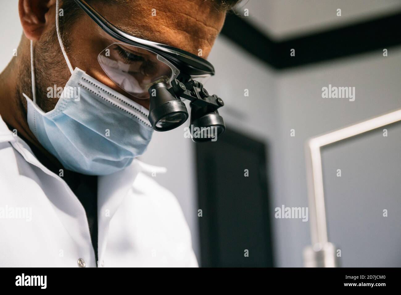 Male dentist wearing mask and surgical loupes while working in clinic ...