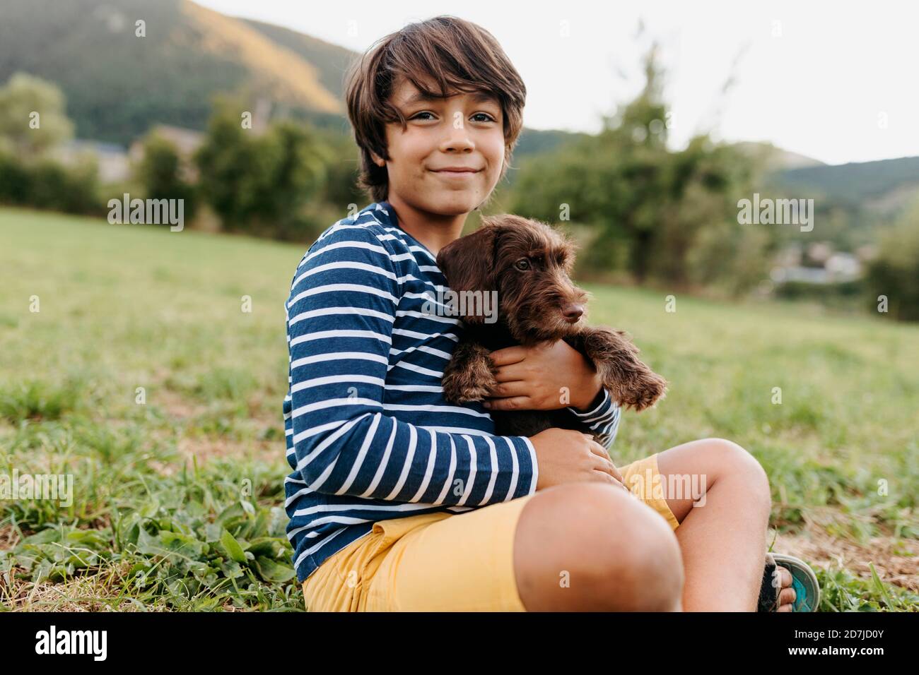 Boy holding puppy while sitting on grass at backyard Stock Photo - Alamy
