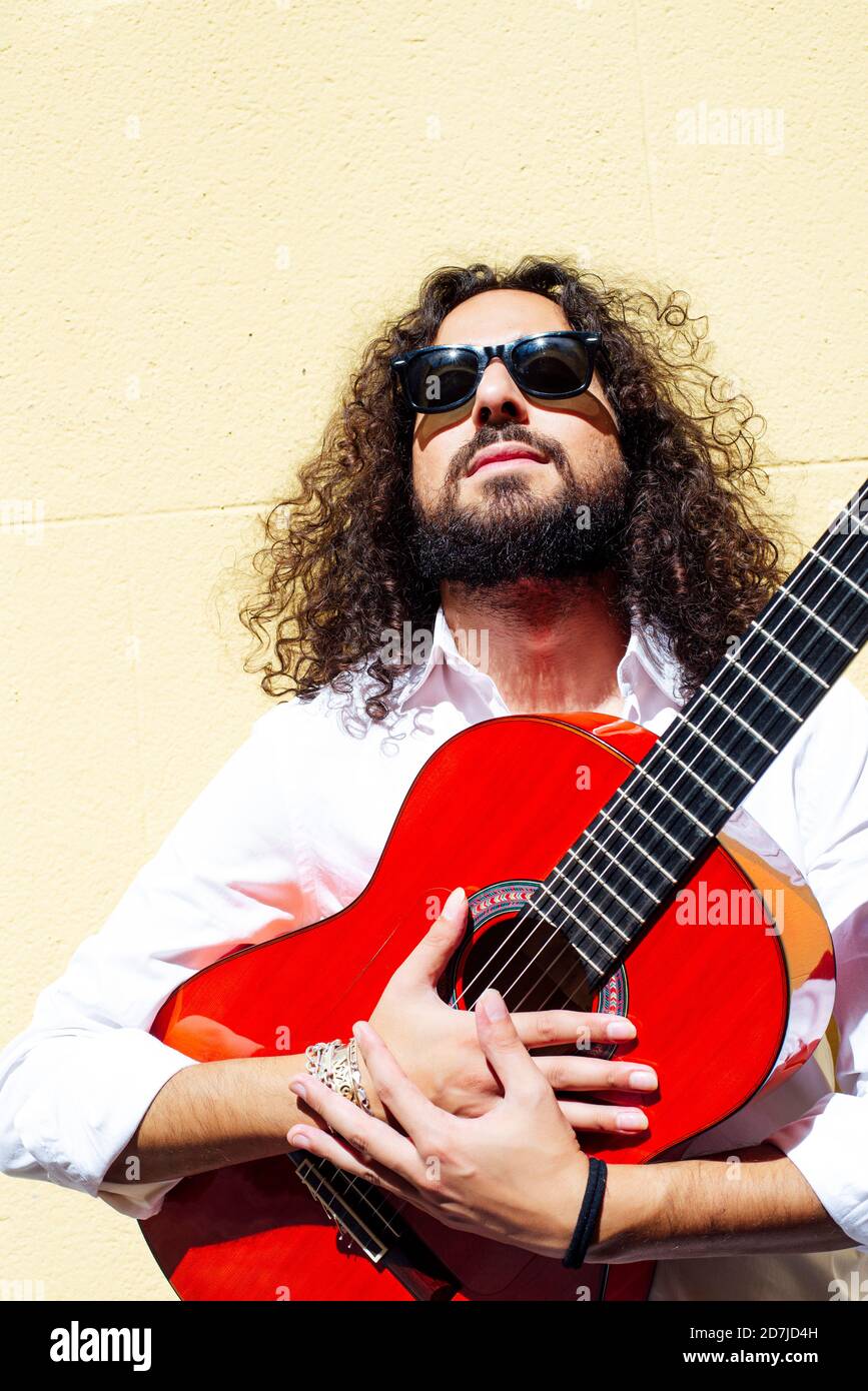 Guitarist holding guitar while standing against yellow wall Stock Photo ...