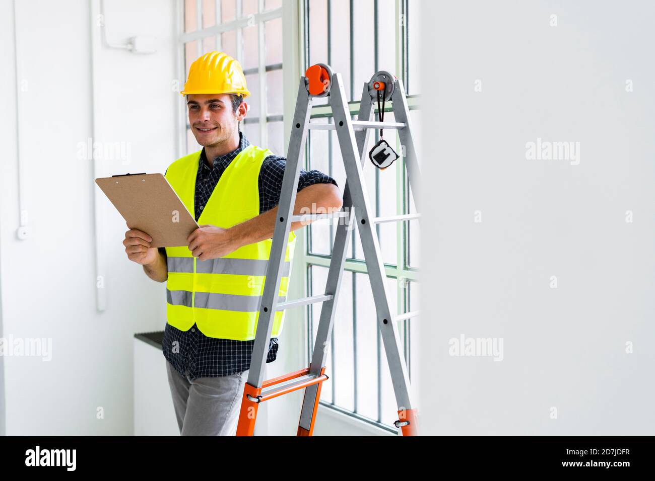 Smiling architect leaning while standing by ladder at office under ...