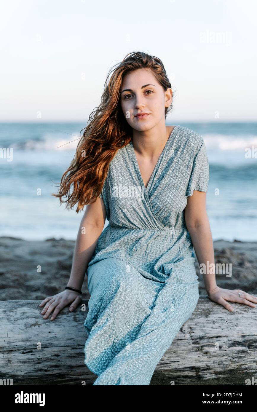 Attractive young woman sitting on log at beach Stock Photo - Alamy