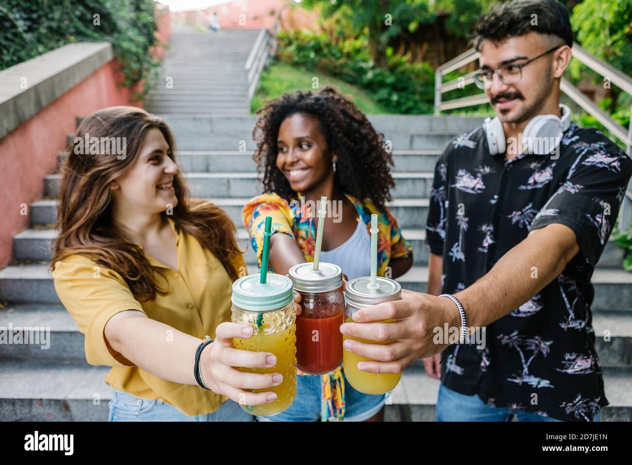 Friends doing celebratory toast while standing against steps in park ...