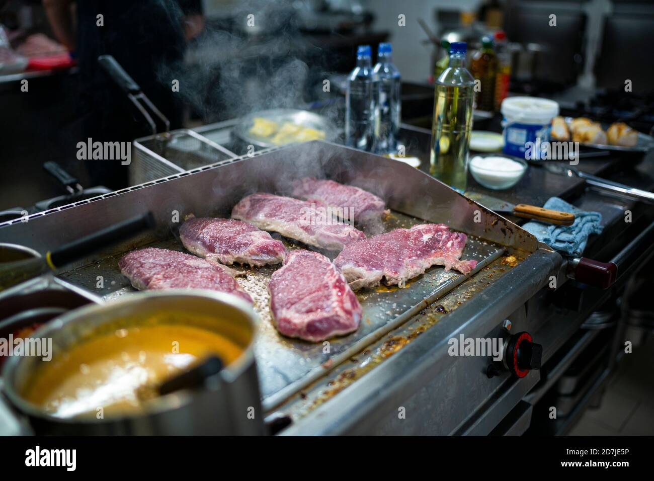 Meat cooking on gas while chef working in background at commercial ...