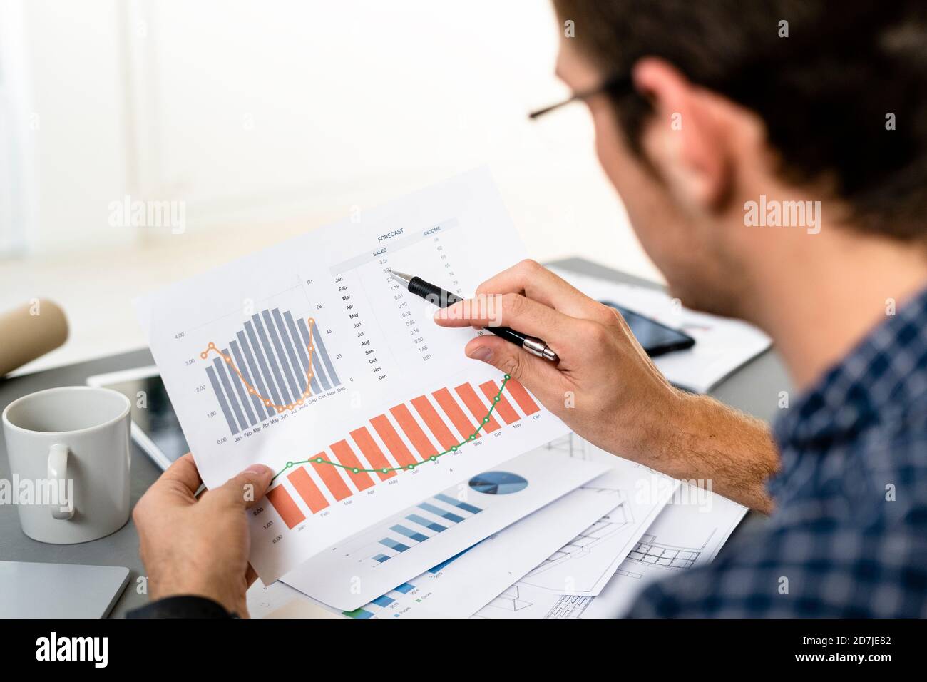 Man analyzing graph paper while sitting by desk at office Stock Photo ...