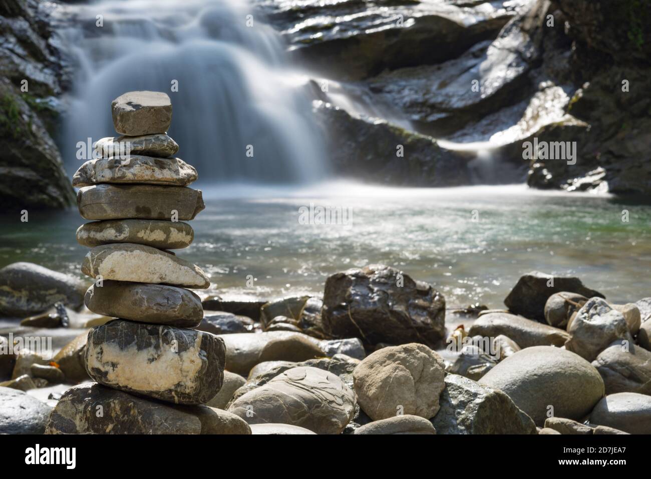 Small cairn with waterfall splashing in background Stock Photo - Alamy
