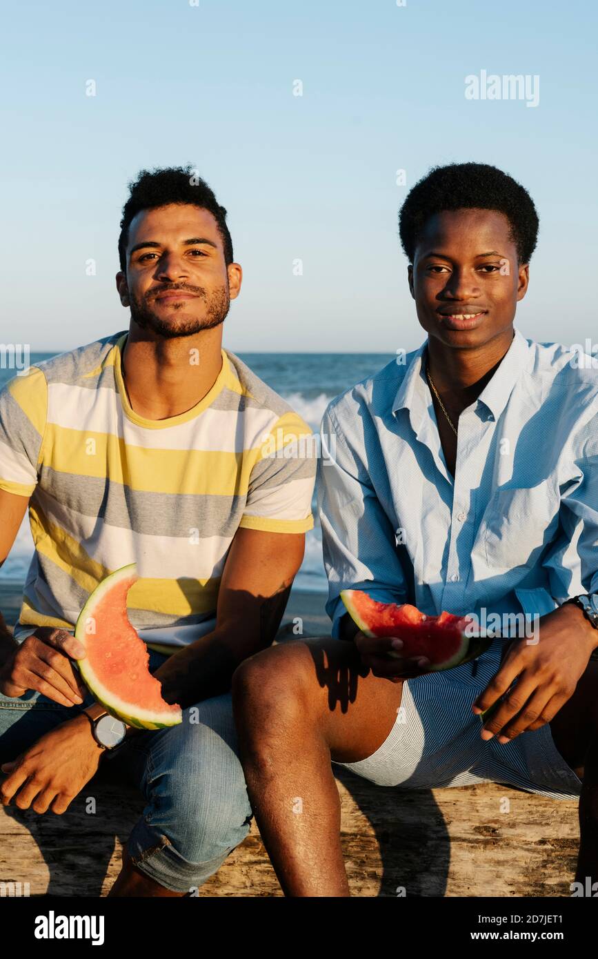 Friends eating watermelon while sitting on beach Stock Photo - Alamy
