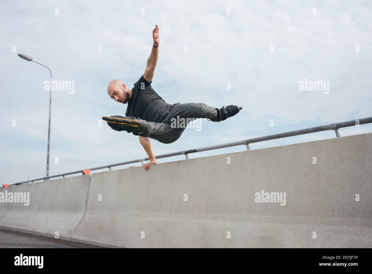 Carefree young man with inline skates jumping over railing on bridge ...