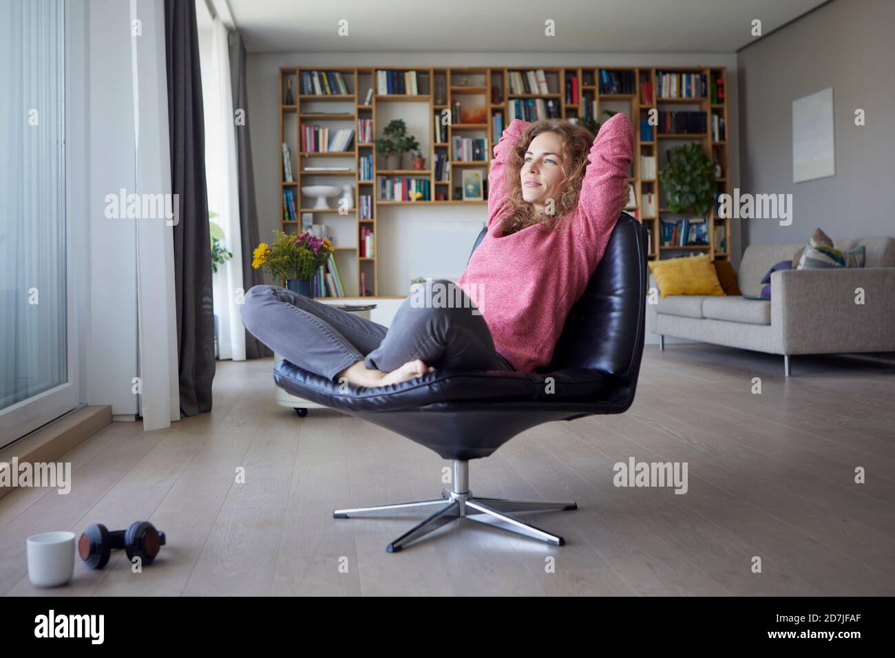 Woman with hands behind head relaxing on chair at home Stock Photo - Alamy