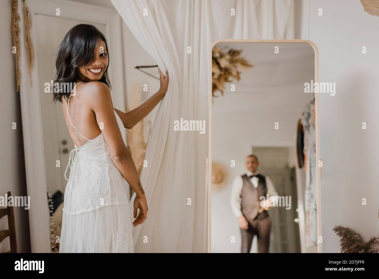 Reflection of bridegroom in mirror while bride looking over shoulder at ...