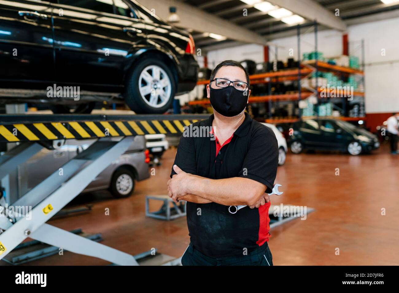Male mechanic wearing mask with arms crossed standing in workshop Stock ...