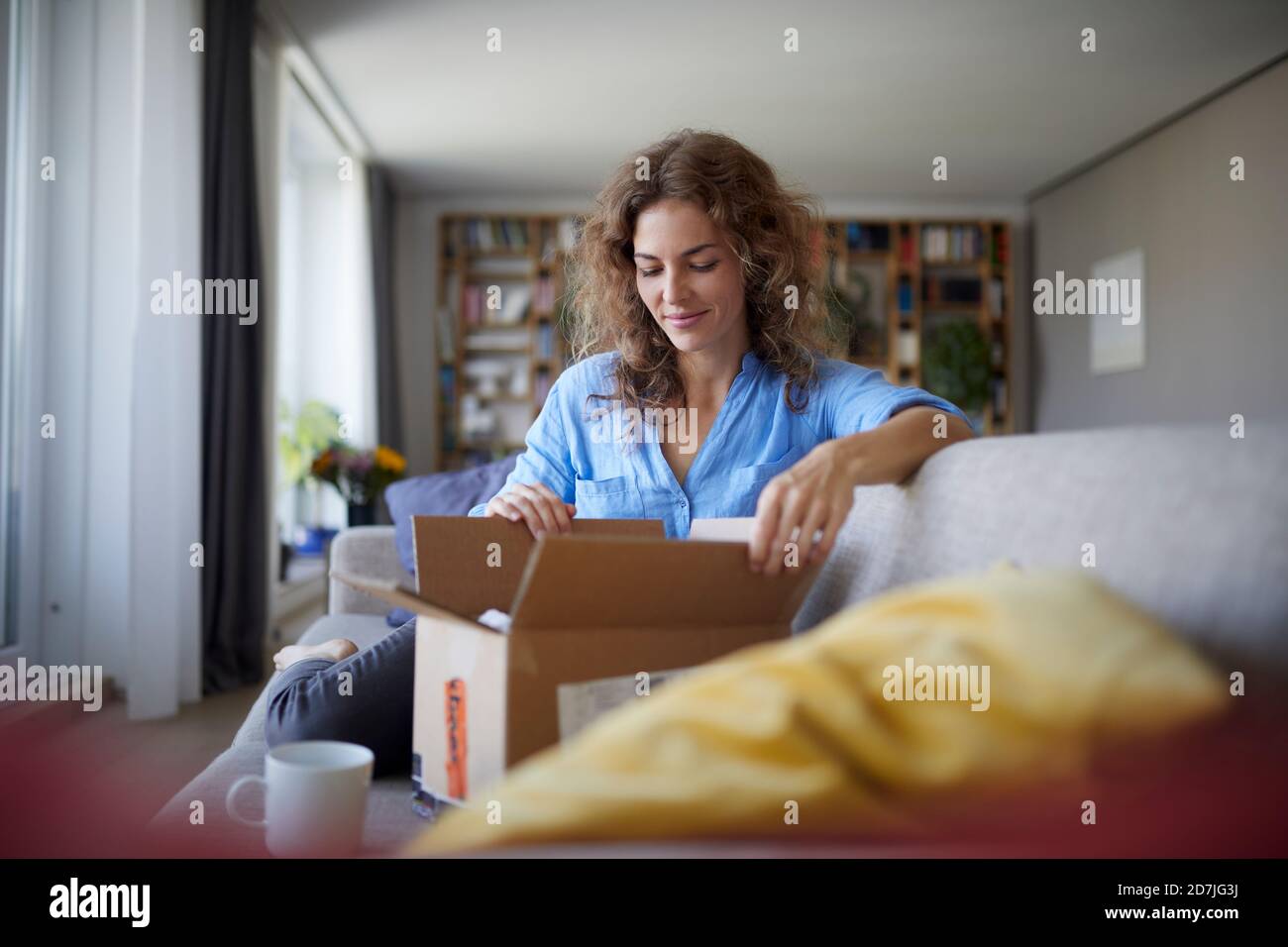 Woman opening box while sitting on sofa at home Stock Photo - Alamy