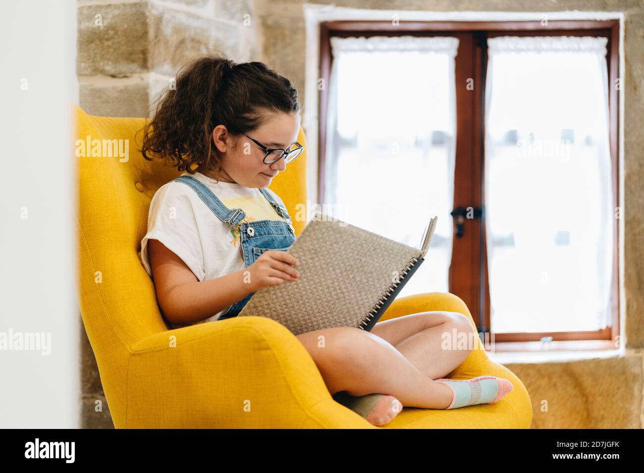 Girl reading book while seating on armchair at home Stock Photo - Alamy