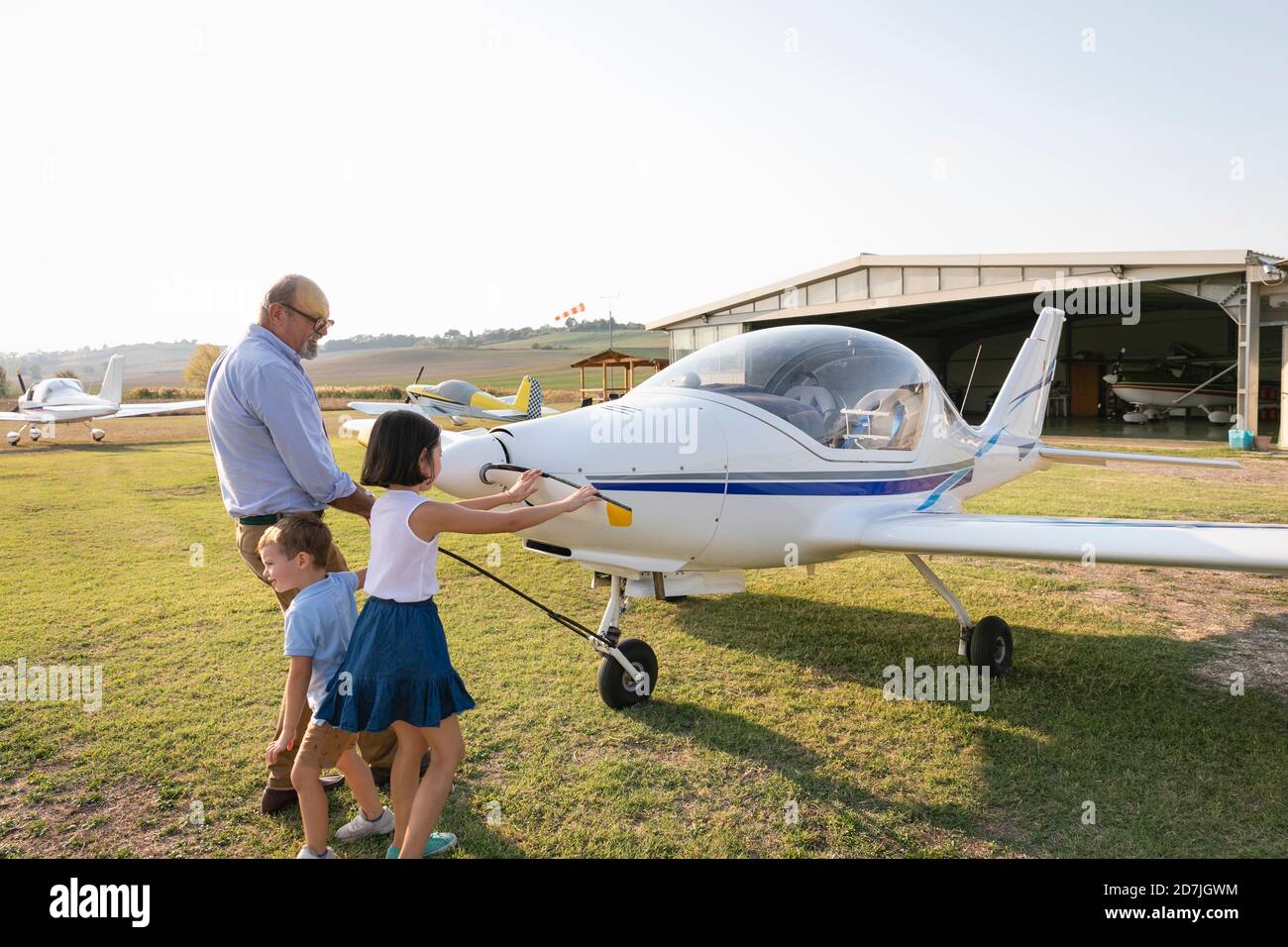 Children and grandfather pulling airplane outside from hangar Stock ...