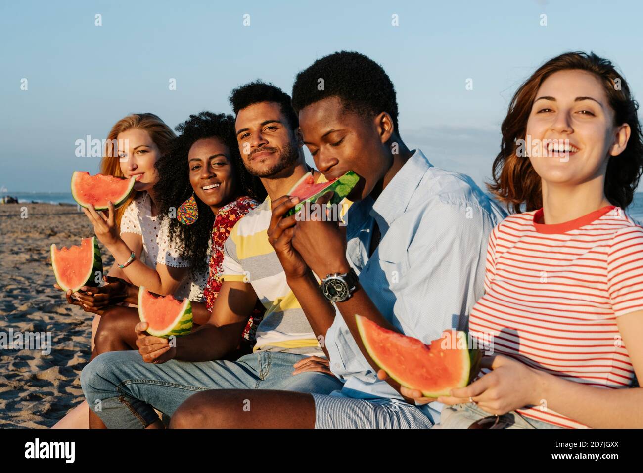Friends enjoying eating slice of watermelon while sitting on beach ...