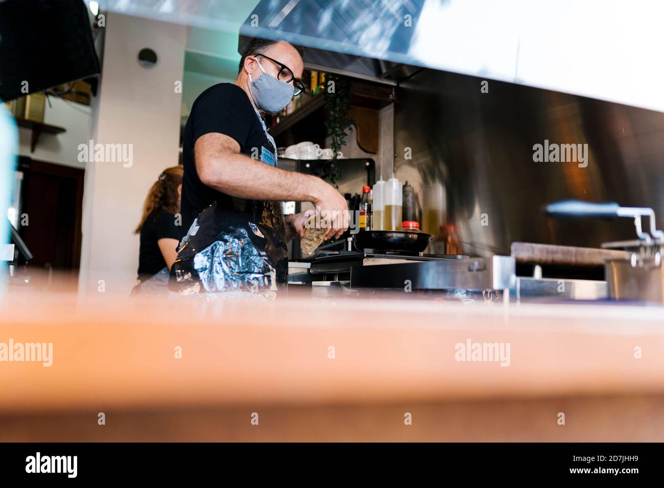 Male barista wearing protective face mask while cooking in kitchen of ...
