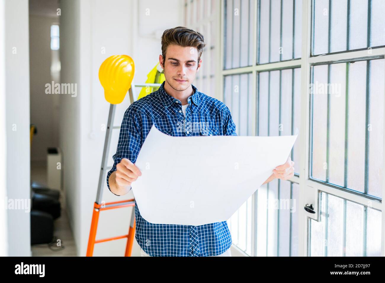 Man holding blueprint while standing by window at office under ...