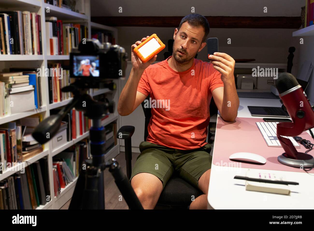 Mid adult man showing external hard disk drive while video recording on ...