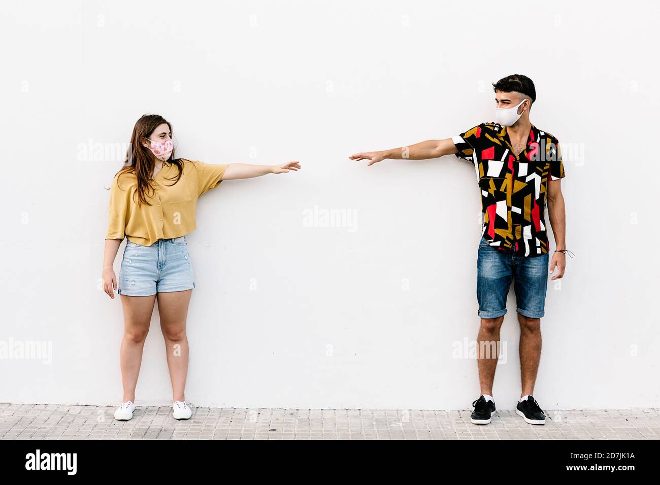 Young friends keeping social distancing while standing against wall ...