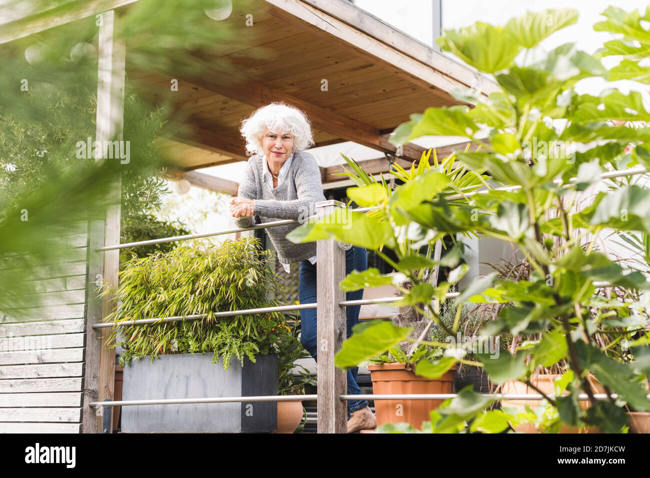 Mature woman leaning on railing while standing at home Stock Photo - Alamy