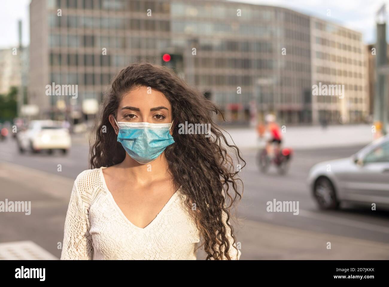 Young woman with wavy hair wearing mask while standing on street in ...
