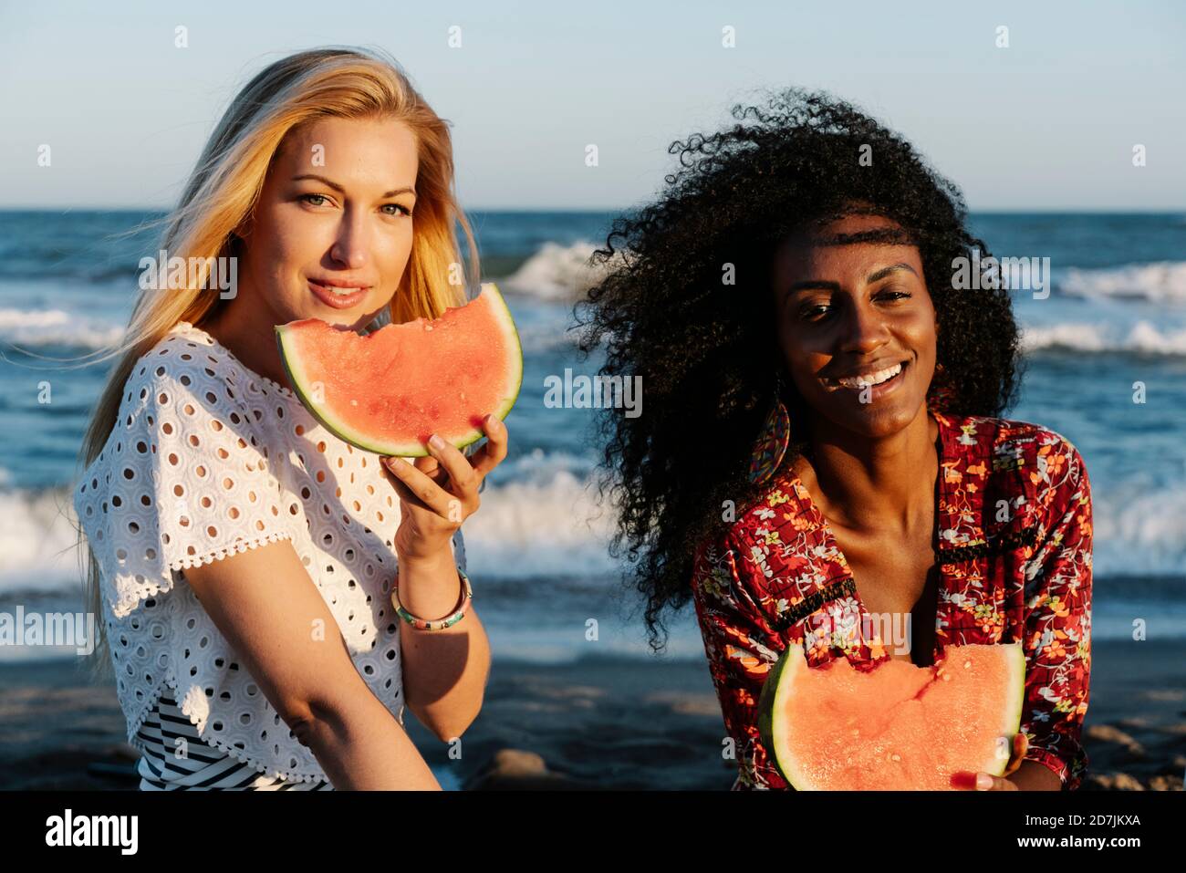 Friends eating slice of watermelon on beach during sunny day Stock ...