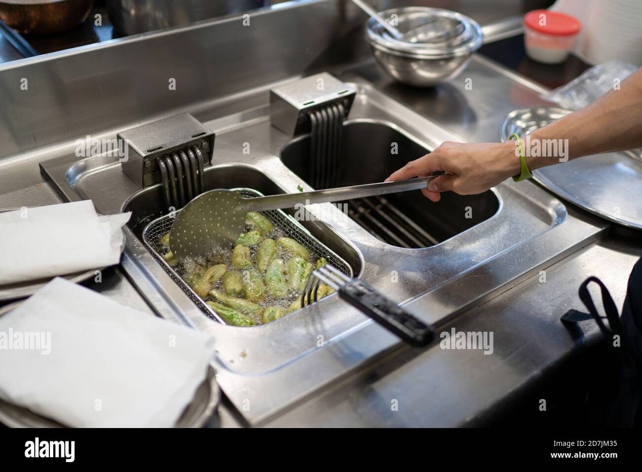 Male chef cooking jalapeno peppers in deep fryer at commercial kitchen ...