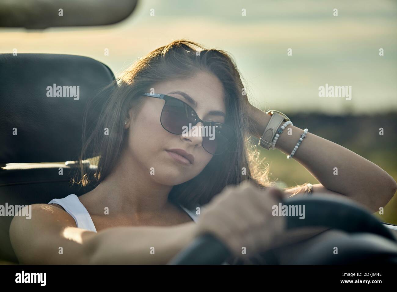 Young woman with hand in hair driving luxury car Stock Photo - Alamy