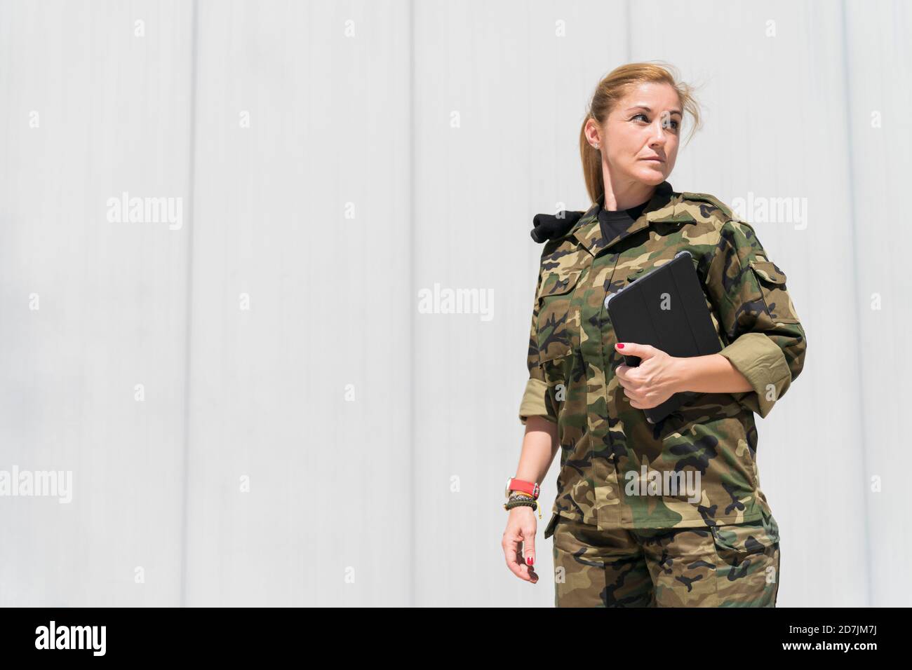 Mature blond female army soldier holding digital tablet while looking ...