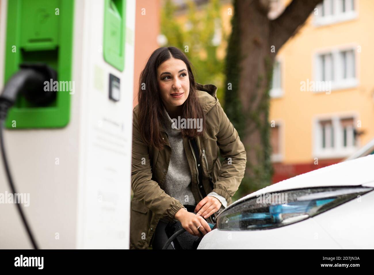 Beautiful woman removing electric plug from car at charging station ...