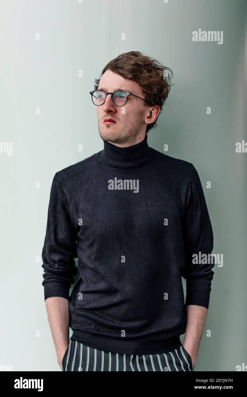 Thoughtful young man with hands in pockets standing against column ...