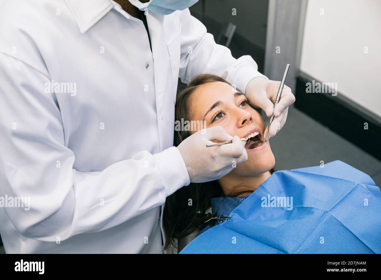 Male dentist inspecting oral cavity of young female patient at clinic ...
