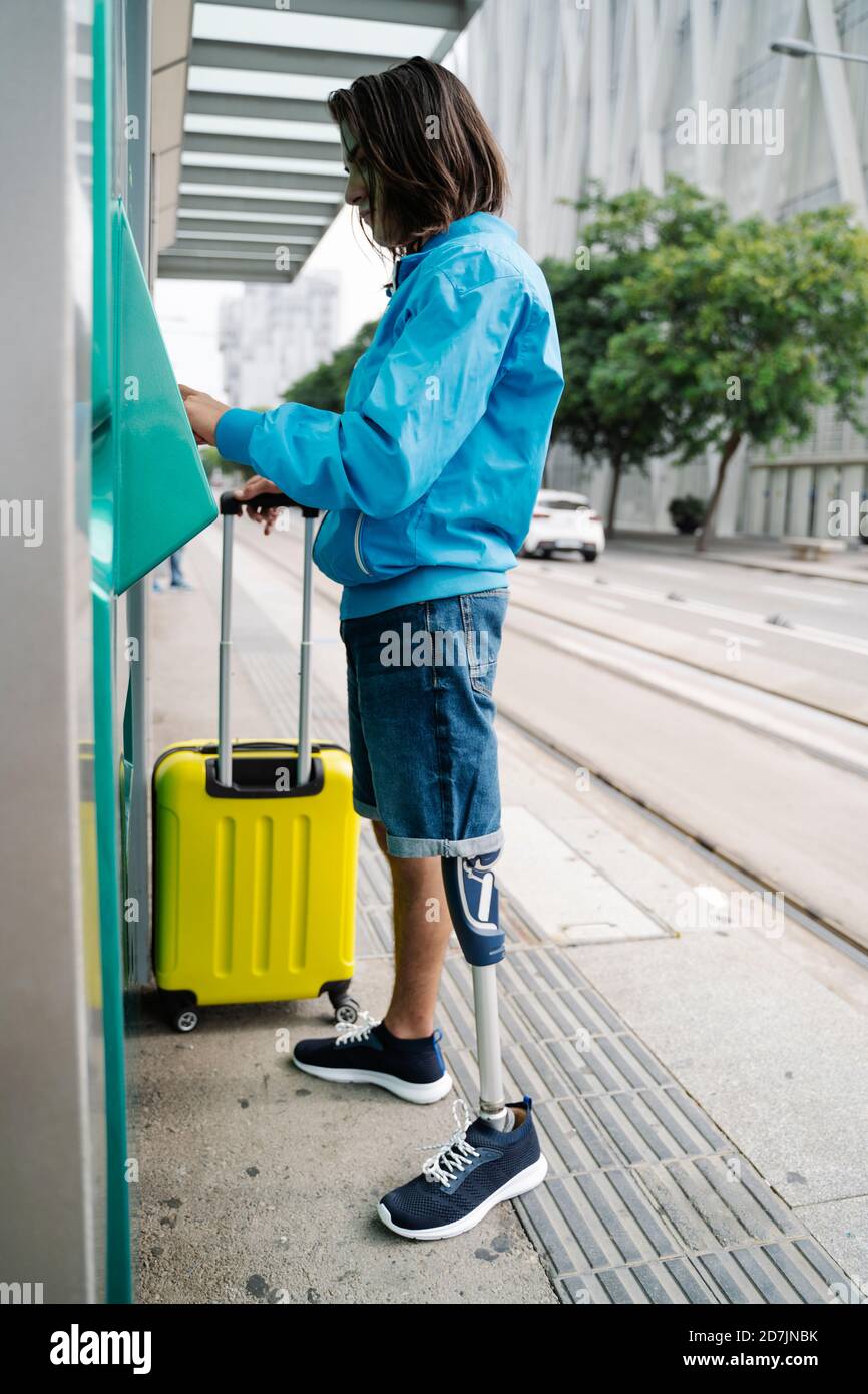 Young man buying ticket from ticket machine while standing at railroad ...