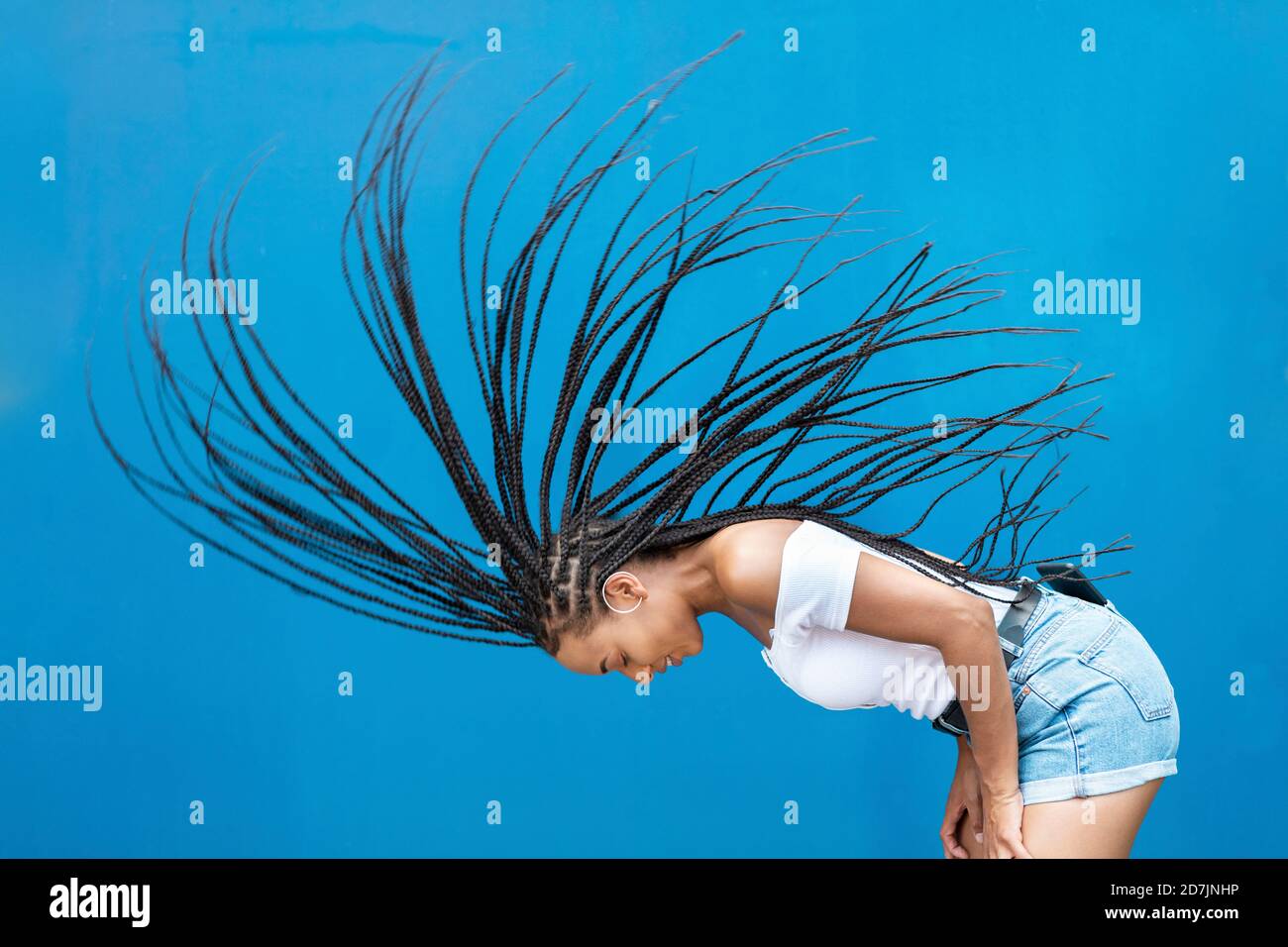 Woman tossing hair against blue wall Stock Photo - Alamy